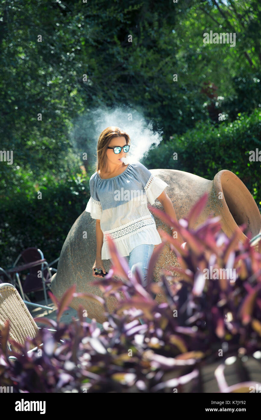 Young woman vaping with sunglasses in a natural scene Stock Photo - Alamy