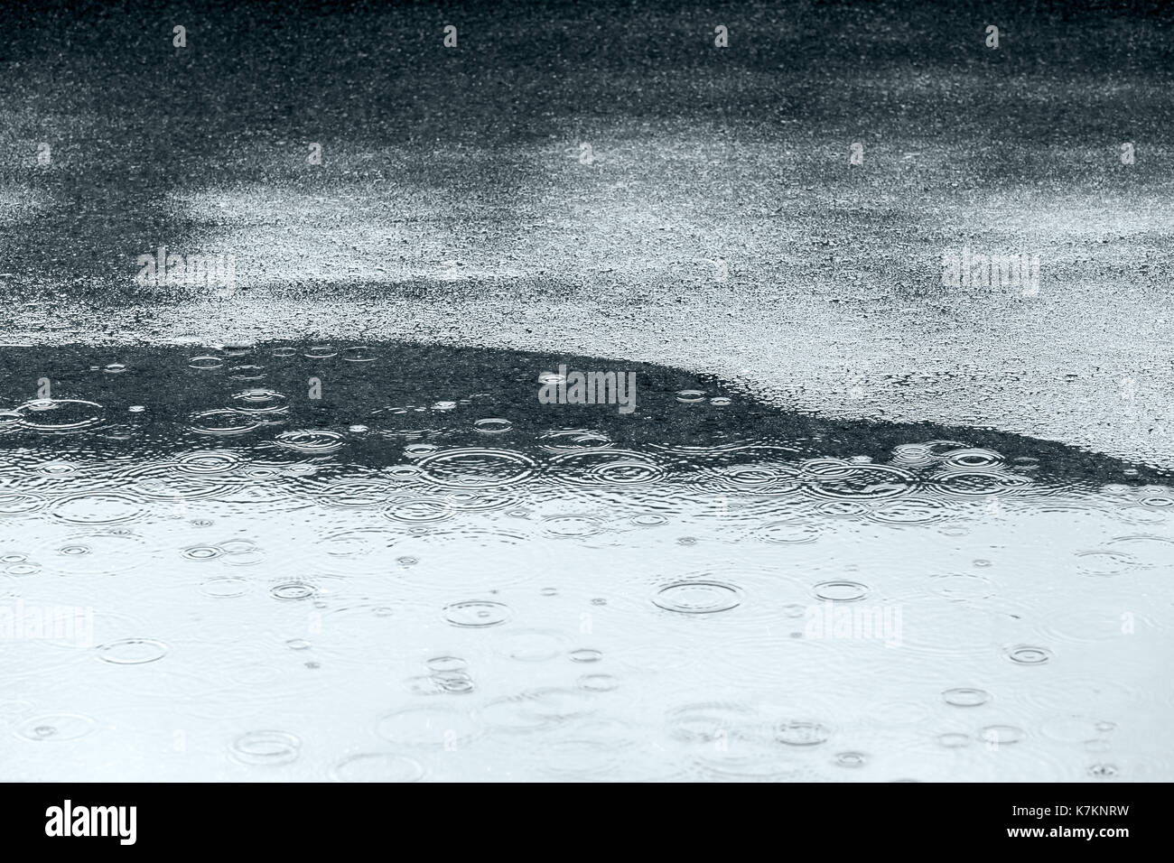 asphalt sidewalk during the rain. raindrops rippling in a water puddle ...