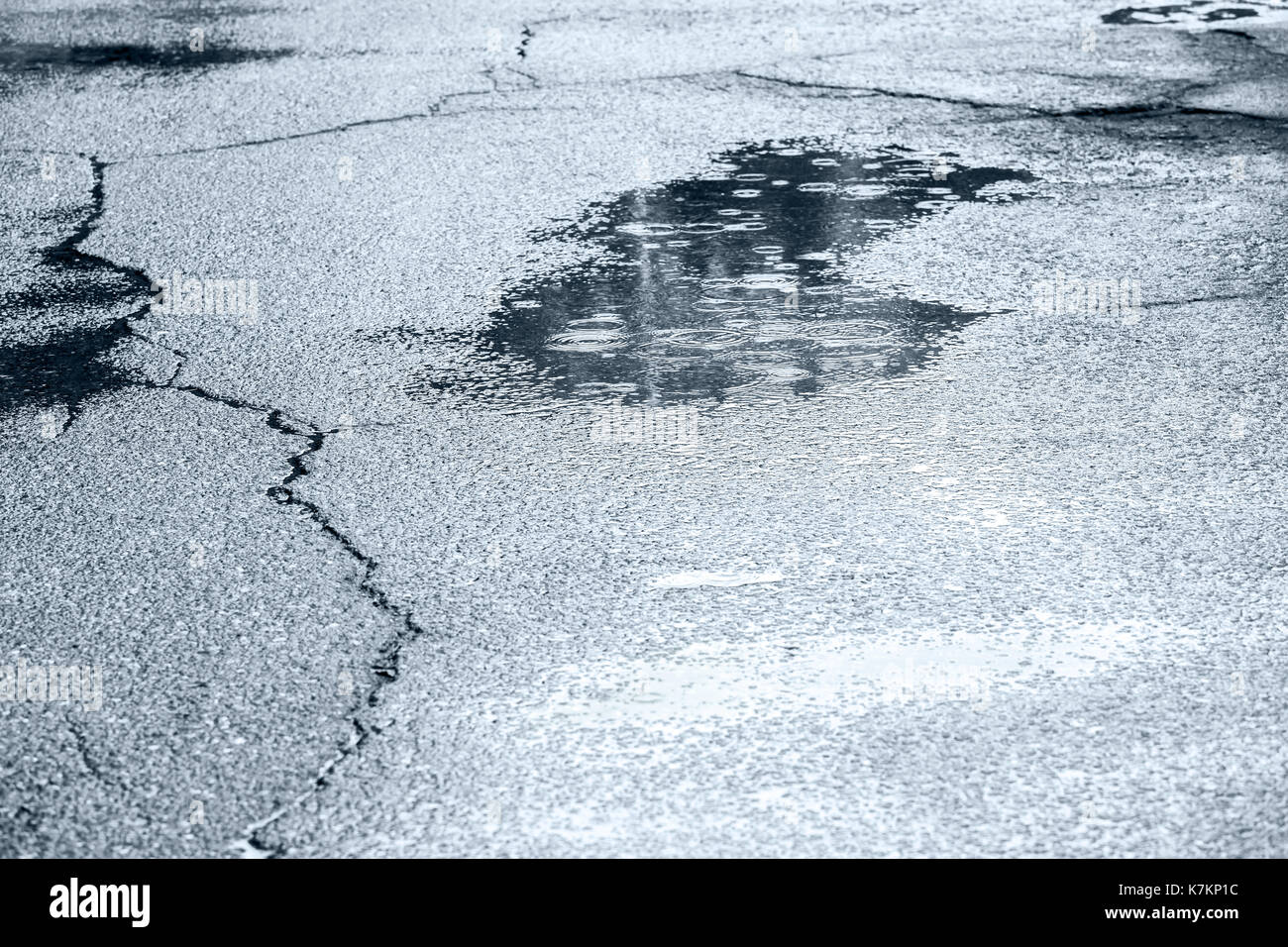 water puddles with raindrops and water circles on cracked wet asphalt ...
