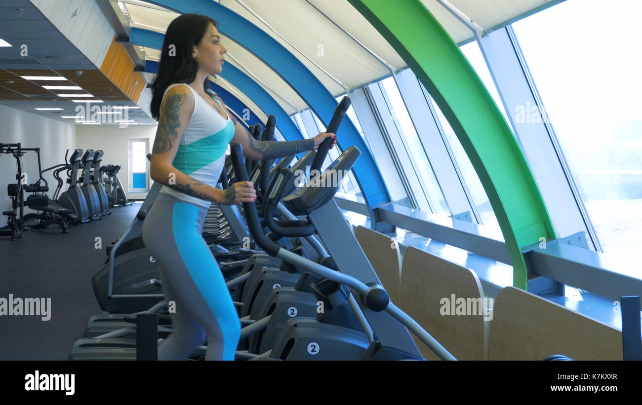 Young fit woman using an elliptic trainer in a fitness center and ...