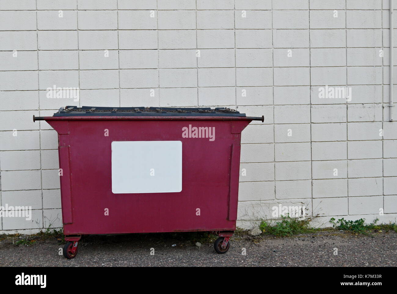 Red recycling dumpster against a white block wall Stock Photo - Alamy