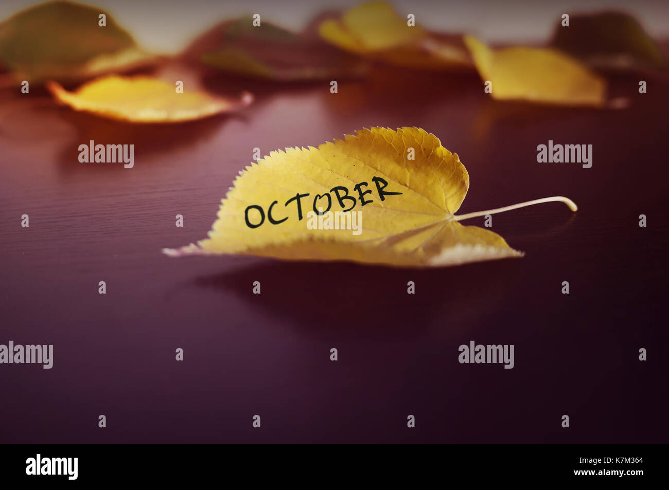 The inscription October on the yellow autumn leaf and a sad face ...