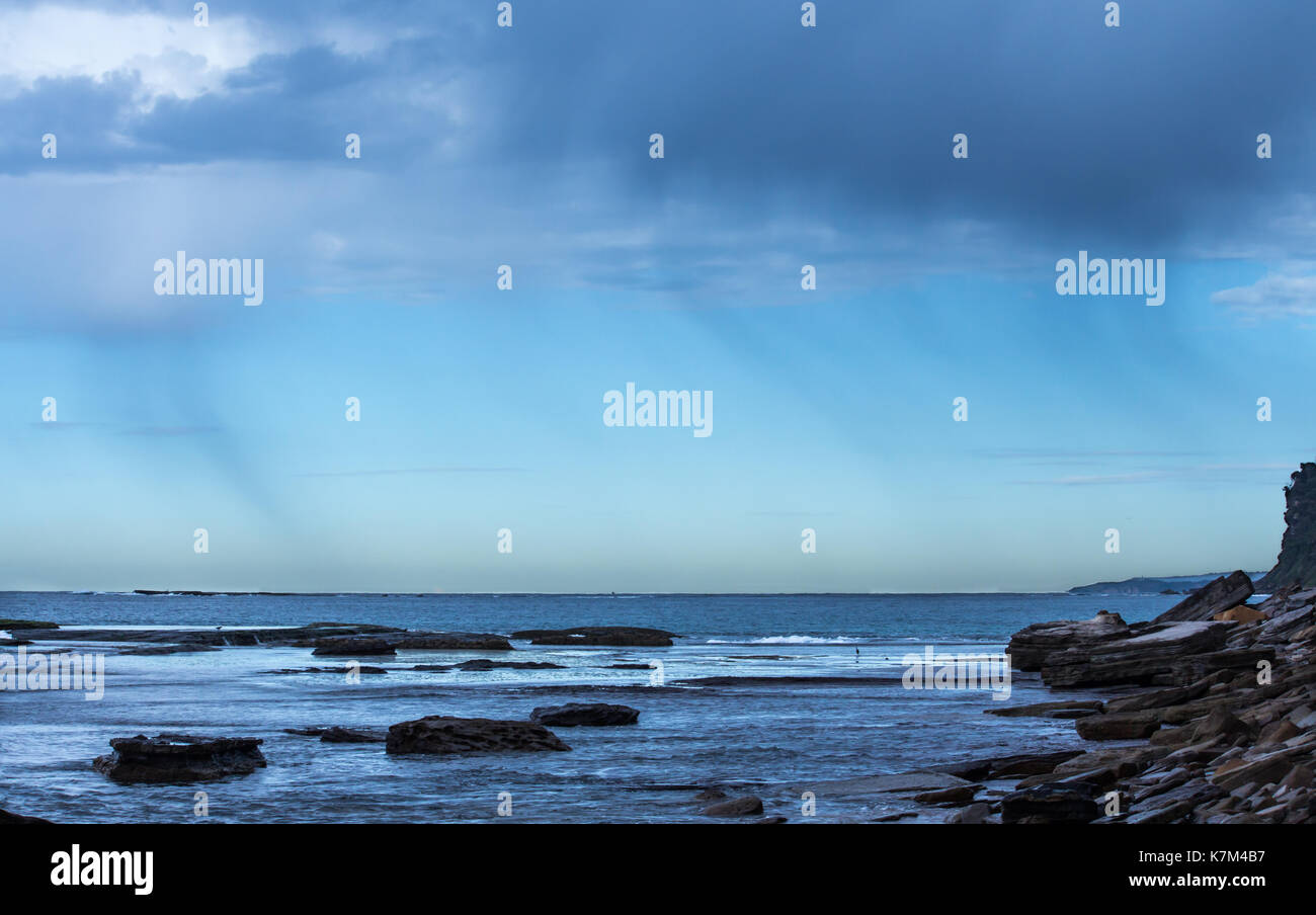 Coastal Rain falling over the ocean against blue sky with seaside rock ...