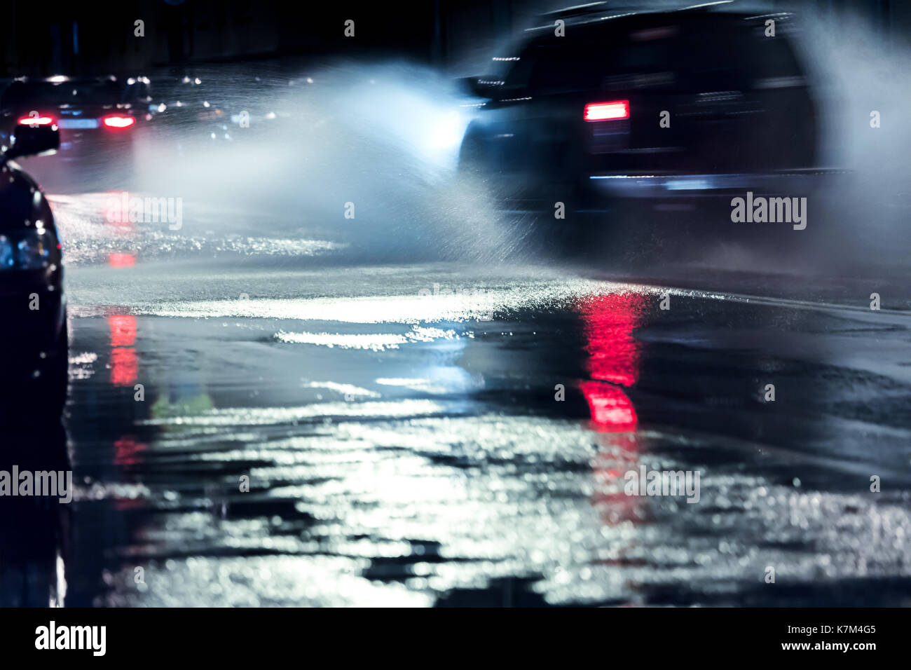 car in motion driving on wet flooded road at night and splashing water ...