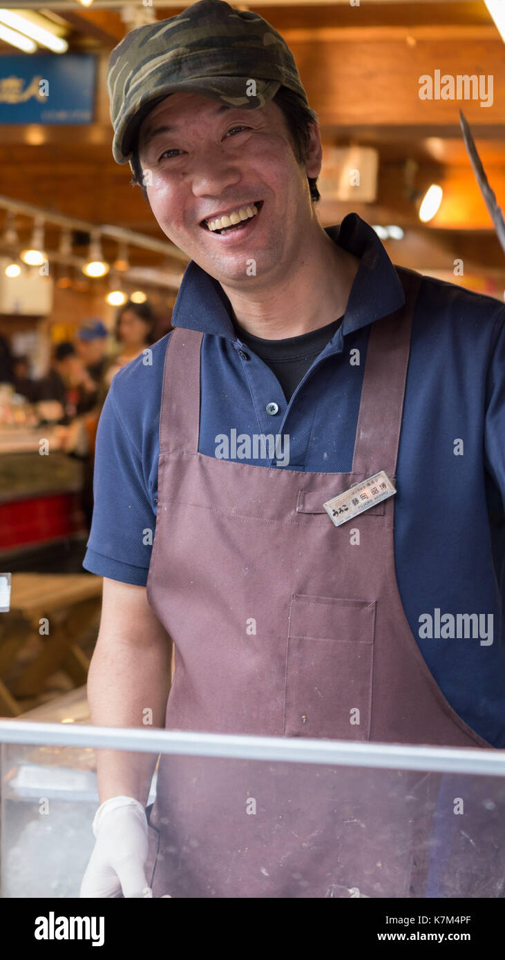 Japanese cracker maker wearing a blue shirt, green cap and purple apron ...