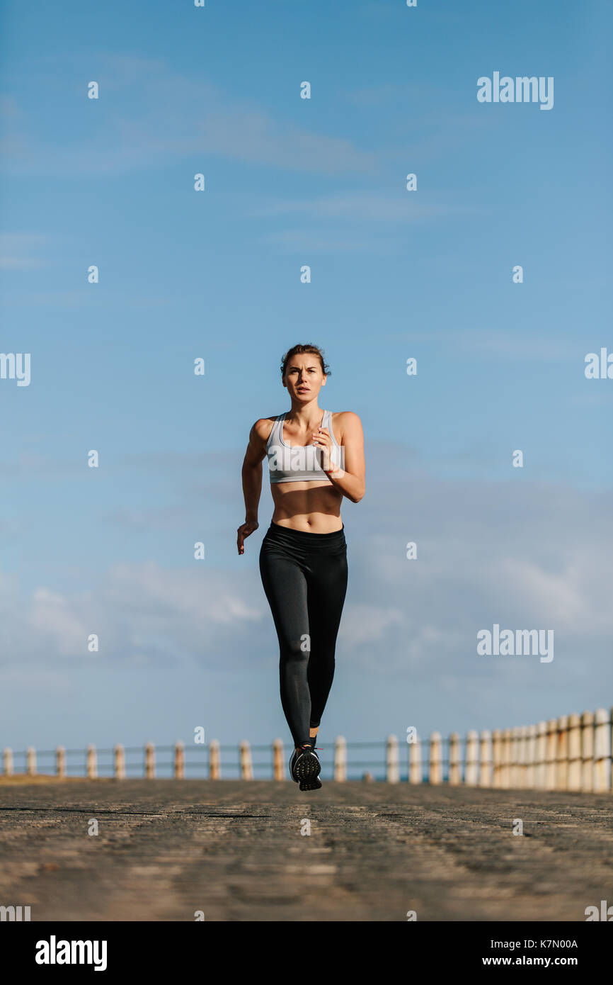 Full length shot of fit young woman running on the seaside promenade ...
