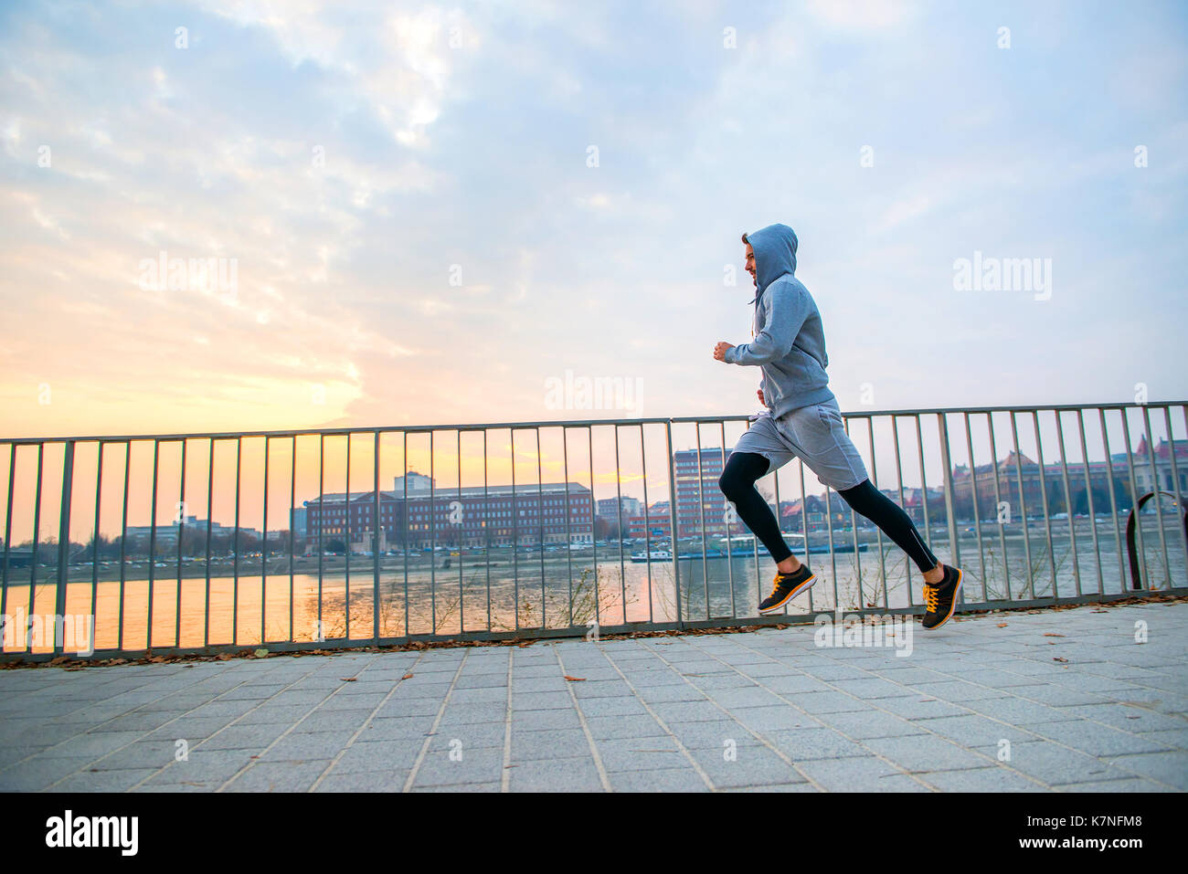A handsome young man running in the sunset next to a fence on the ...