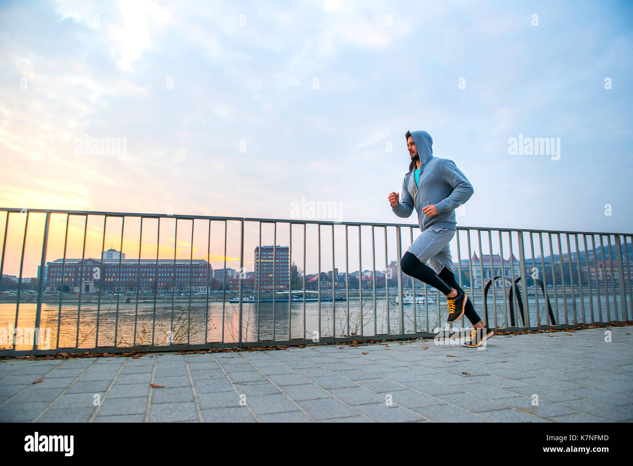A handsome young man running in the sunset next to a fence on the ...