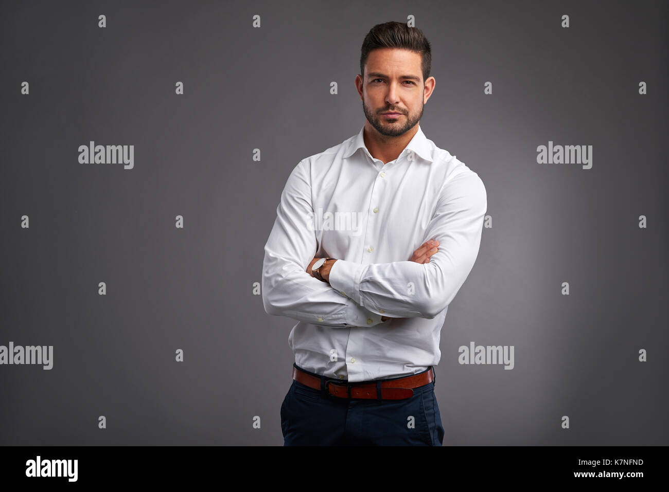 A handsome confident young man standing seriously in a white shirt ...
