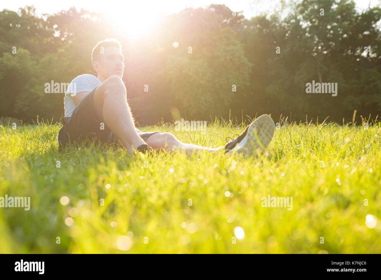 A handsome young man relaxing in the sunset and sitting in the grass ...