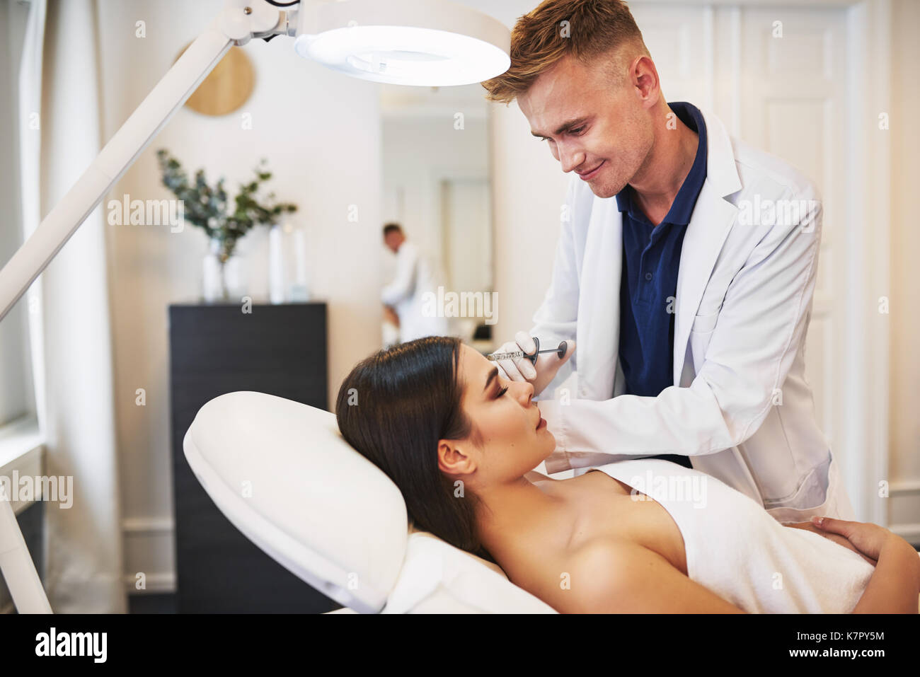 Male doctor performing a botox injection to the forehead of a young ...