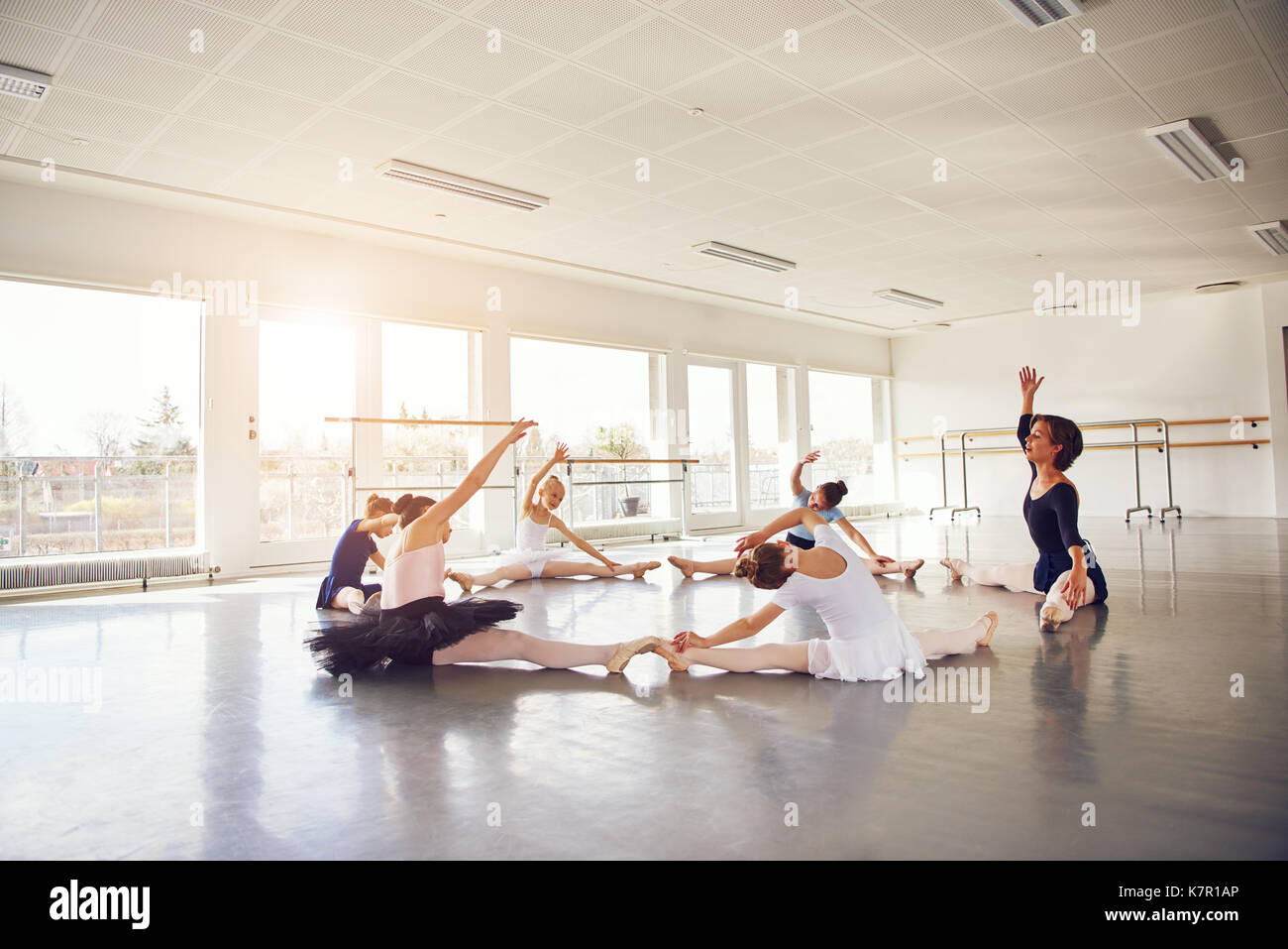 Little ballerinas sitting and doing string exercise with teacher in ...