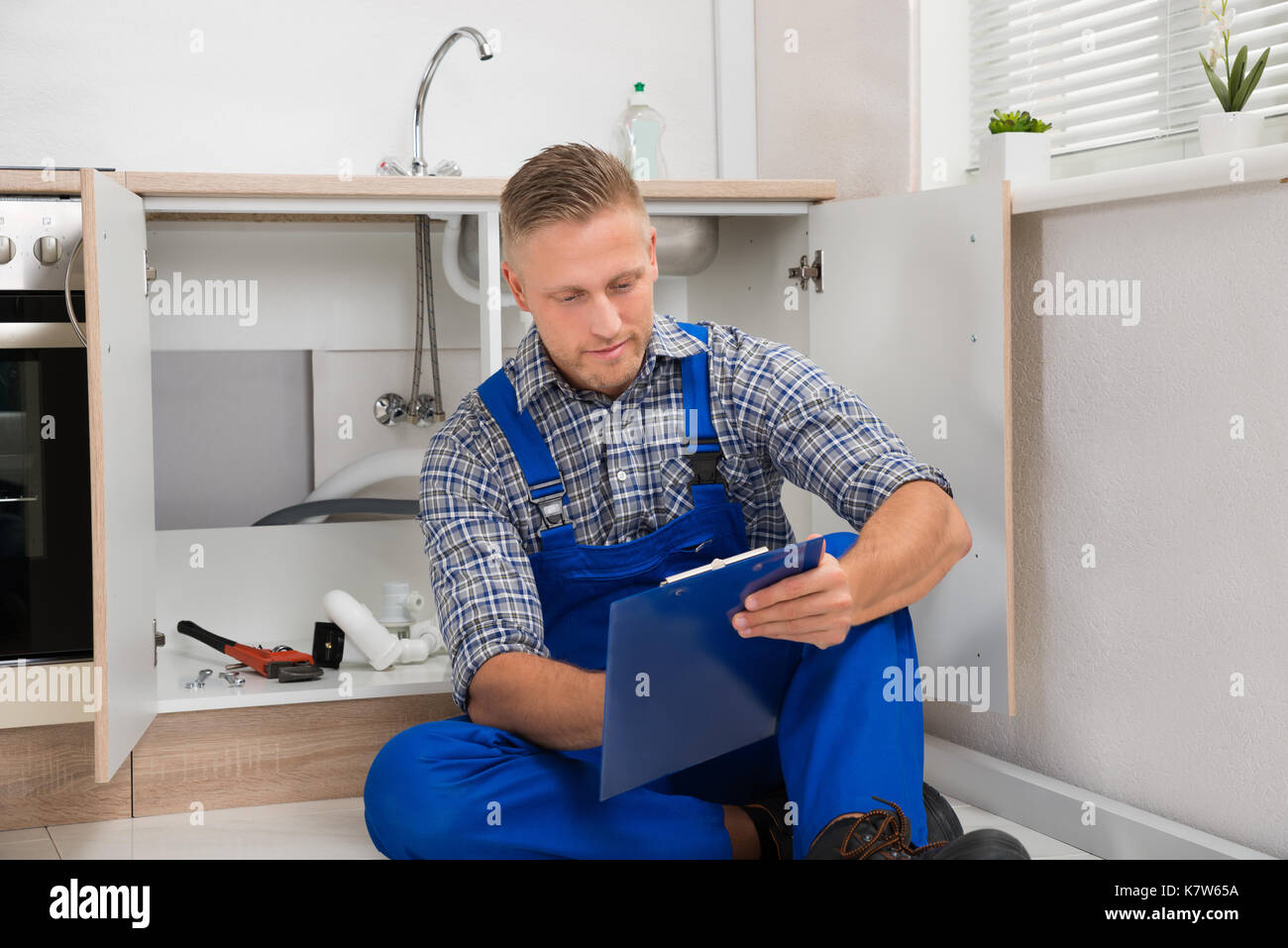 Young Plumber Looking At Clipboard In Kitchen Room Stock Photo - Alamy