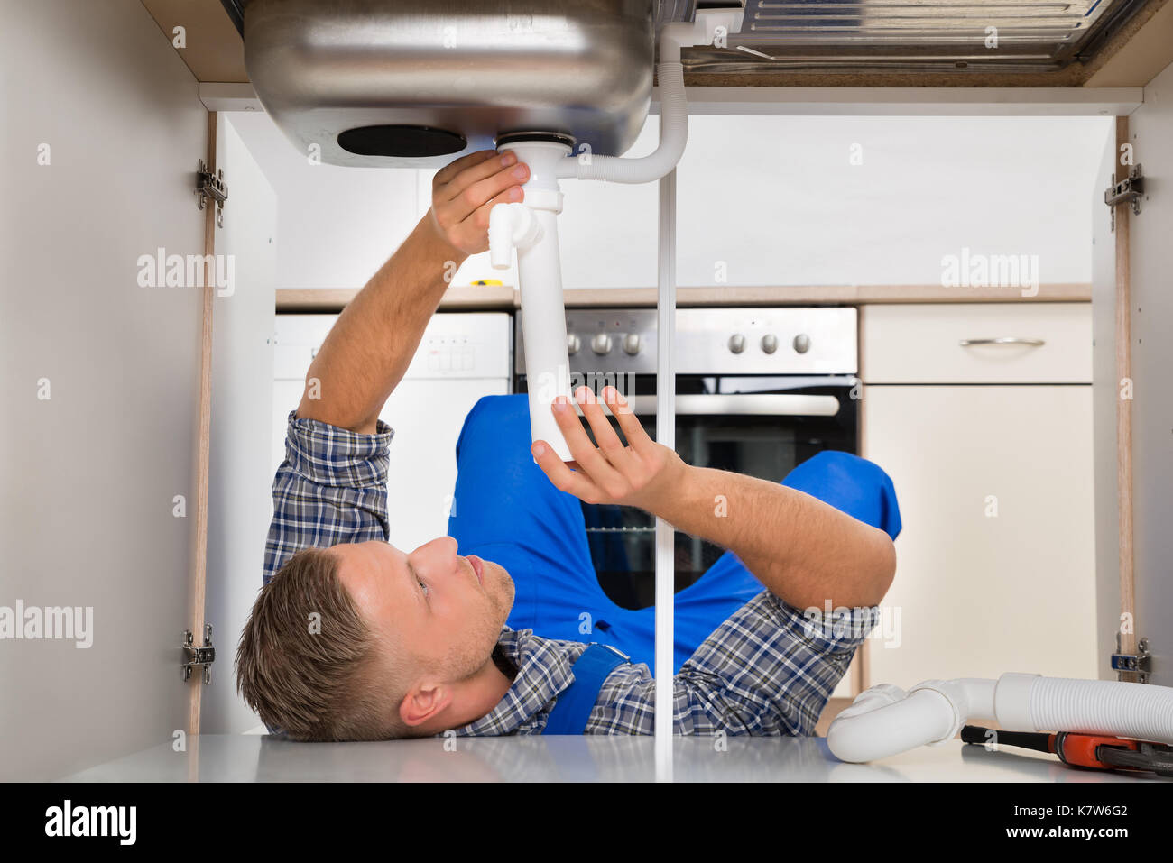 Male Plumber Lying On Floor While Fixing Pipe Into The Steel Sink Stock ...