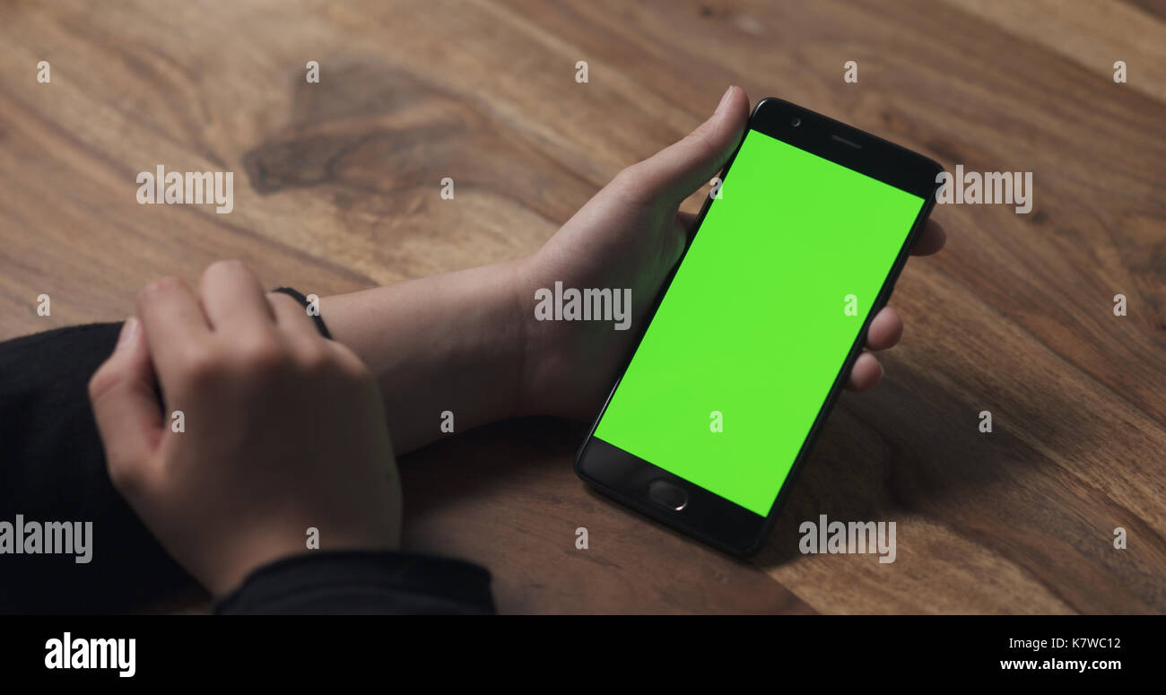 female teen girl hold smartphone with green screen over wood table ...
