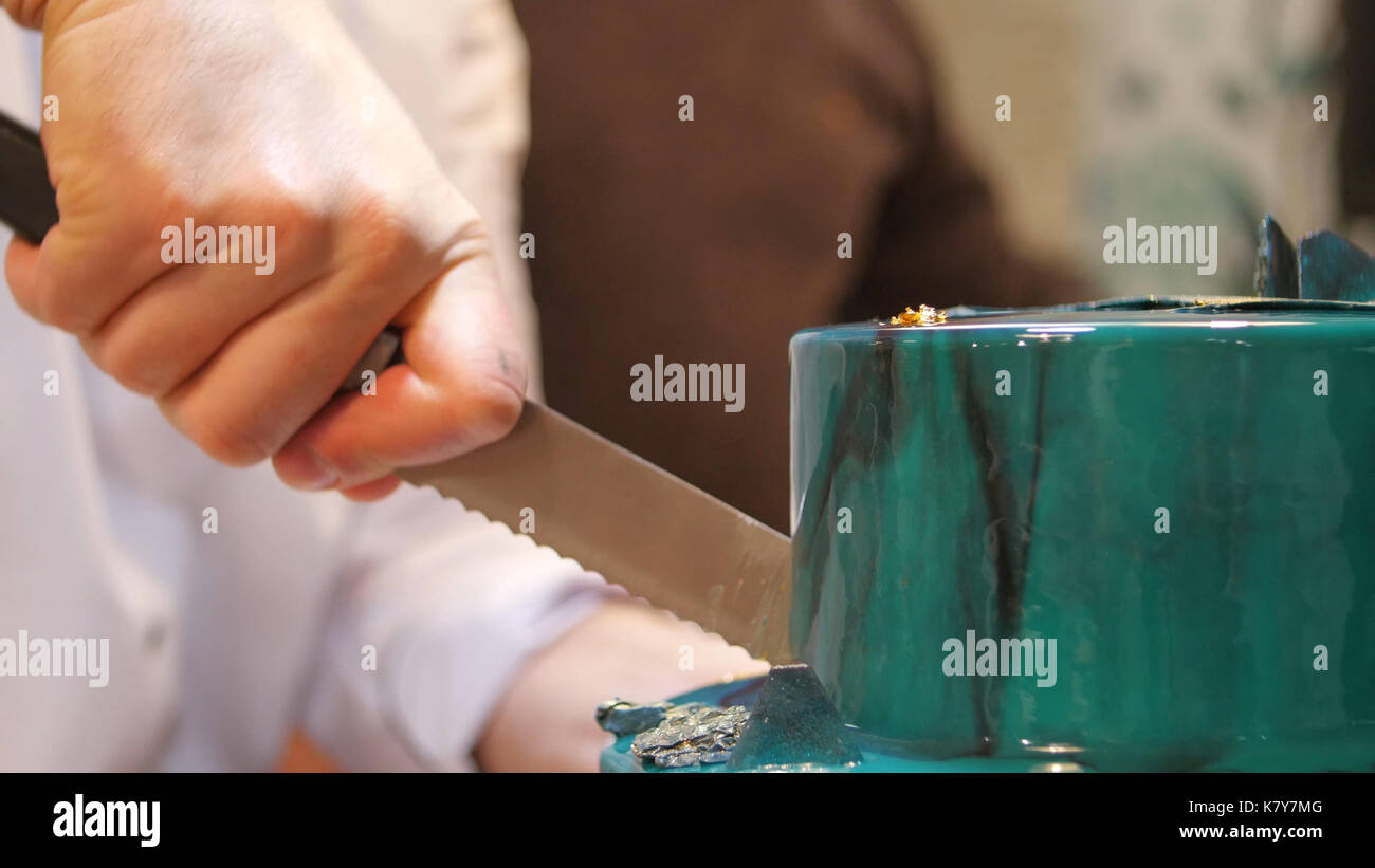 The pastry chef cut the cake with a long knife. Cut a turquoise cake ...