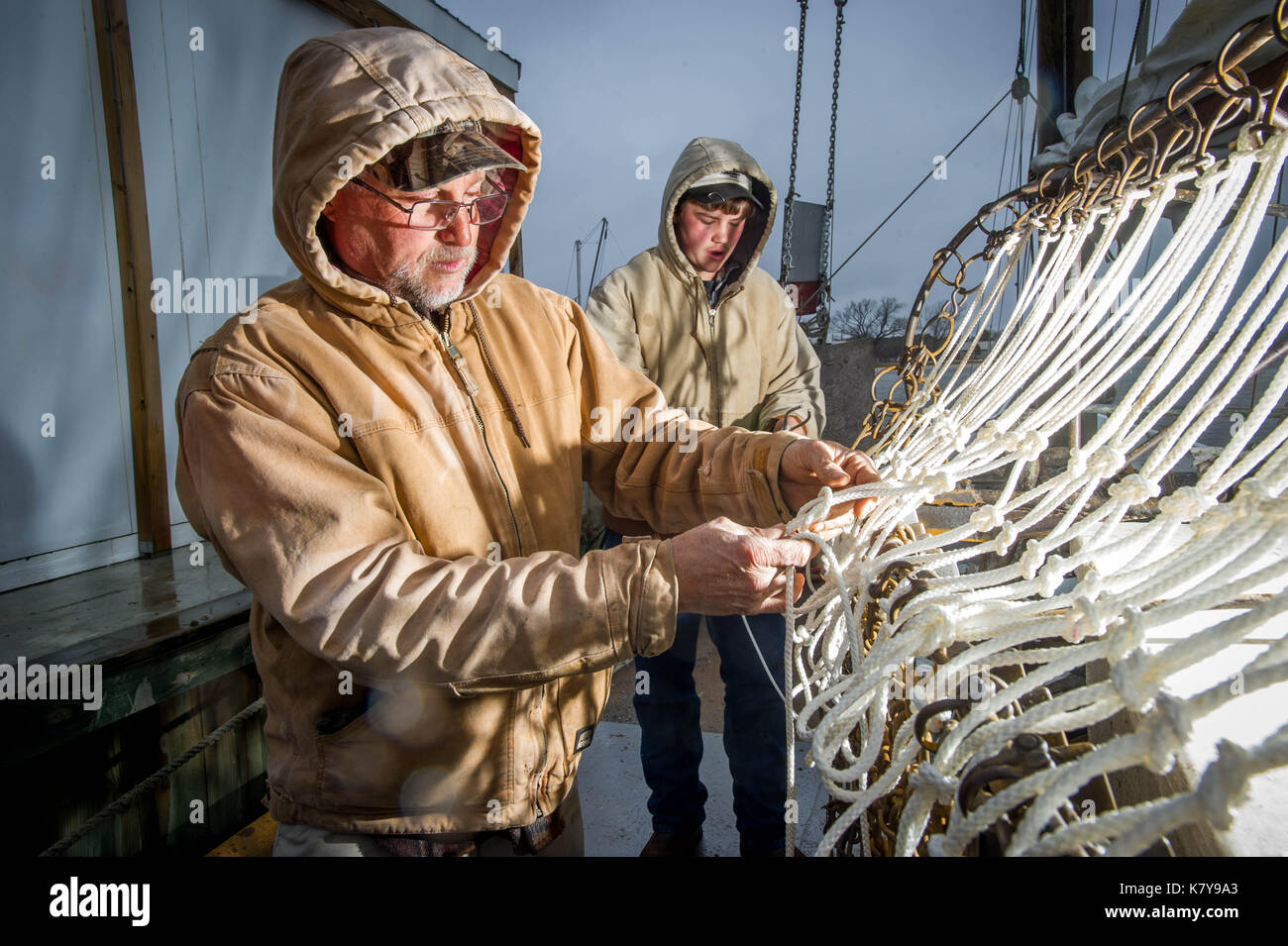 Captain shows son how to tie knots on oyster dredging net aboard ...