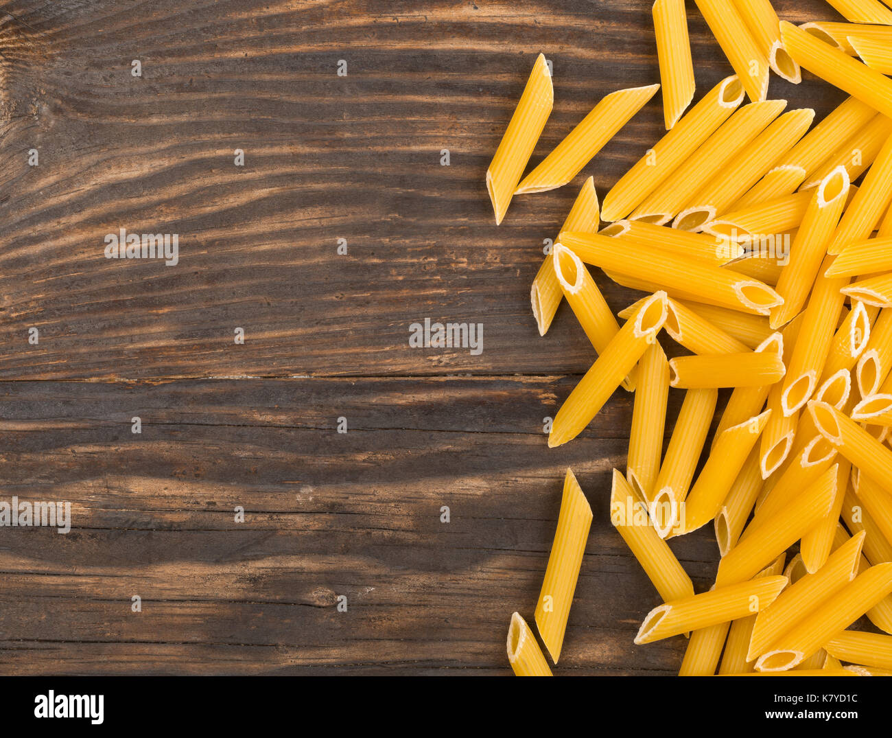 Raw, uncooked, dry penne pasta noodles border on rustic brown wooden ...