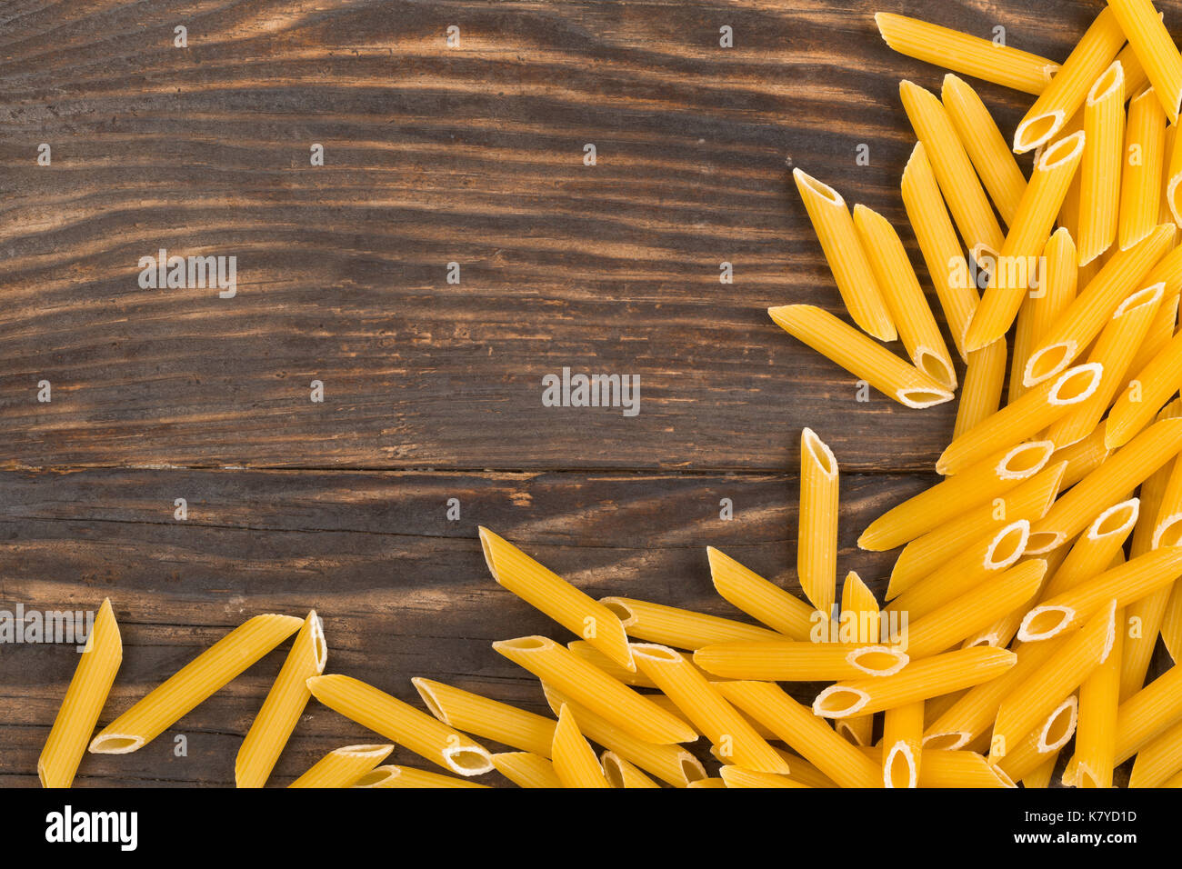 Raw, uncooked, dry penne pasta noodles border on rustic brown wooden ...