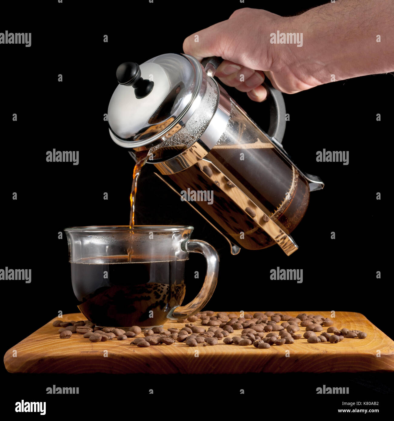 Coffee press made of glass moves coffee into a cup with beens on a ...