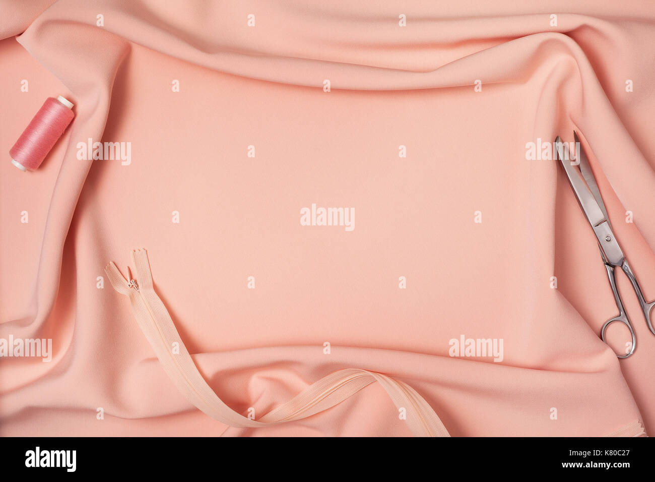 background of peach fabric drapery, scissors, thread, zipper. view from ...