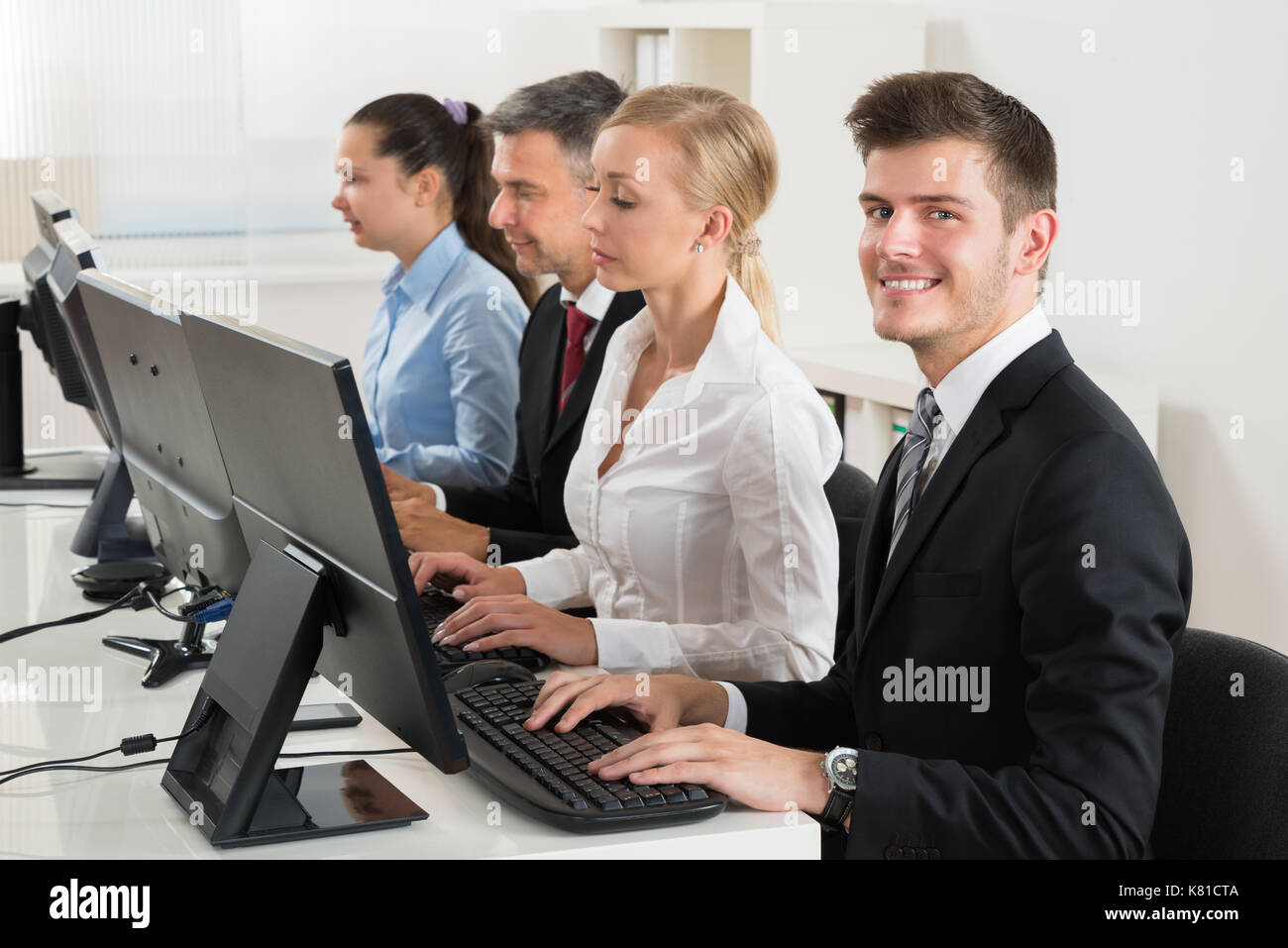 Group Of Businesspeople Typing On Desktop Computer At Desk Stock Photo ...