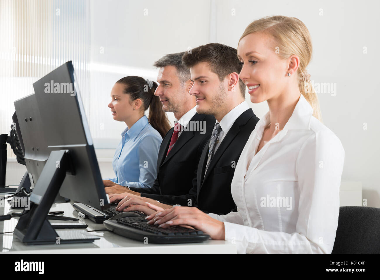 Group Of Businesspeople Typing On Desktop Computer At Desk Stock Photo ...