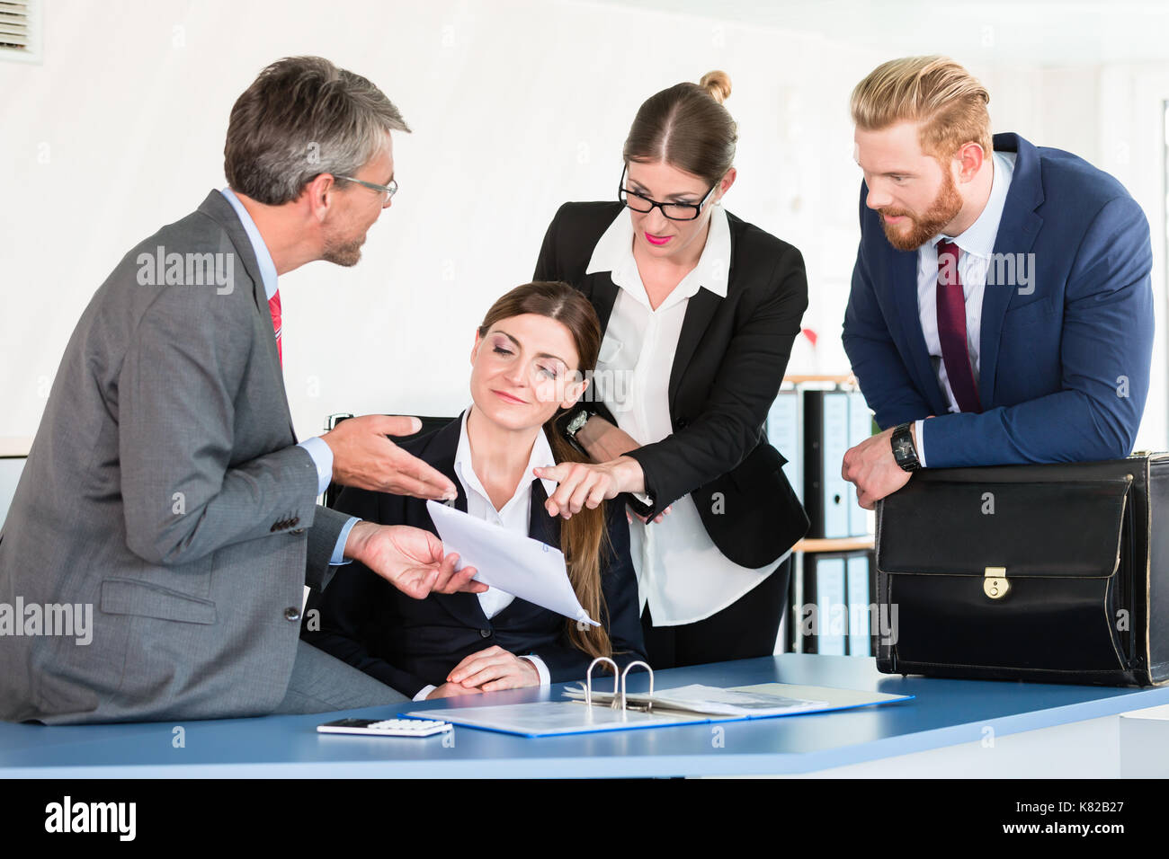 Team gathers around a desk, discussing a document Stock Photo - Alamy