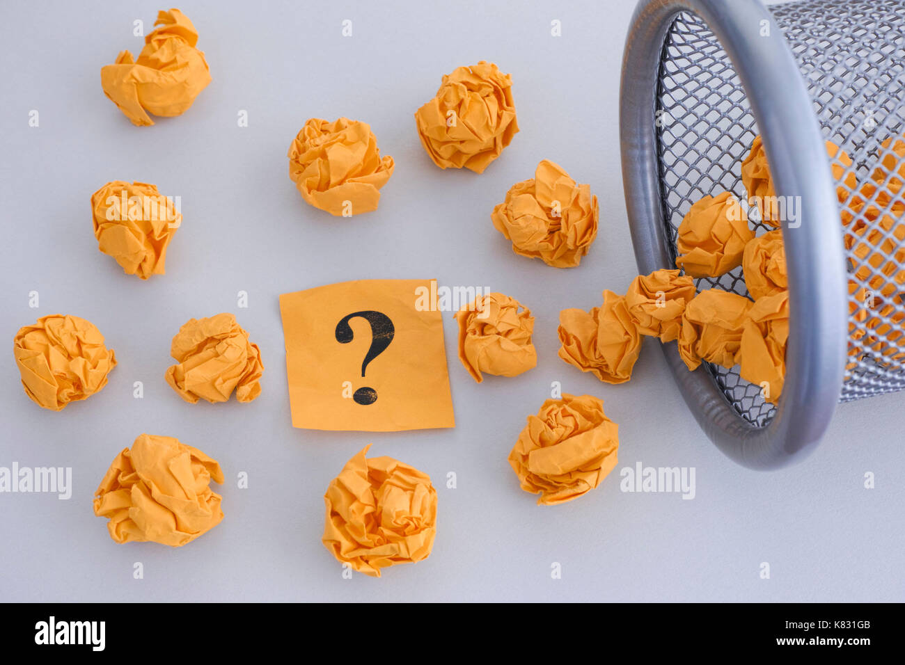 Yellow crumpled paper balls and question mark rolling out of a trash ...