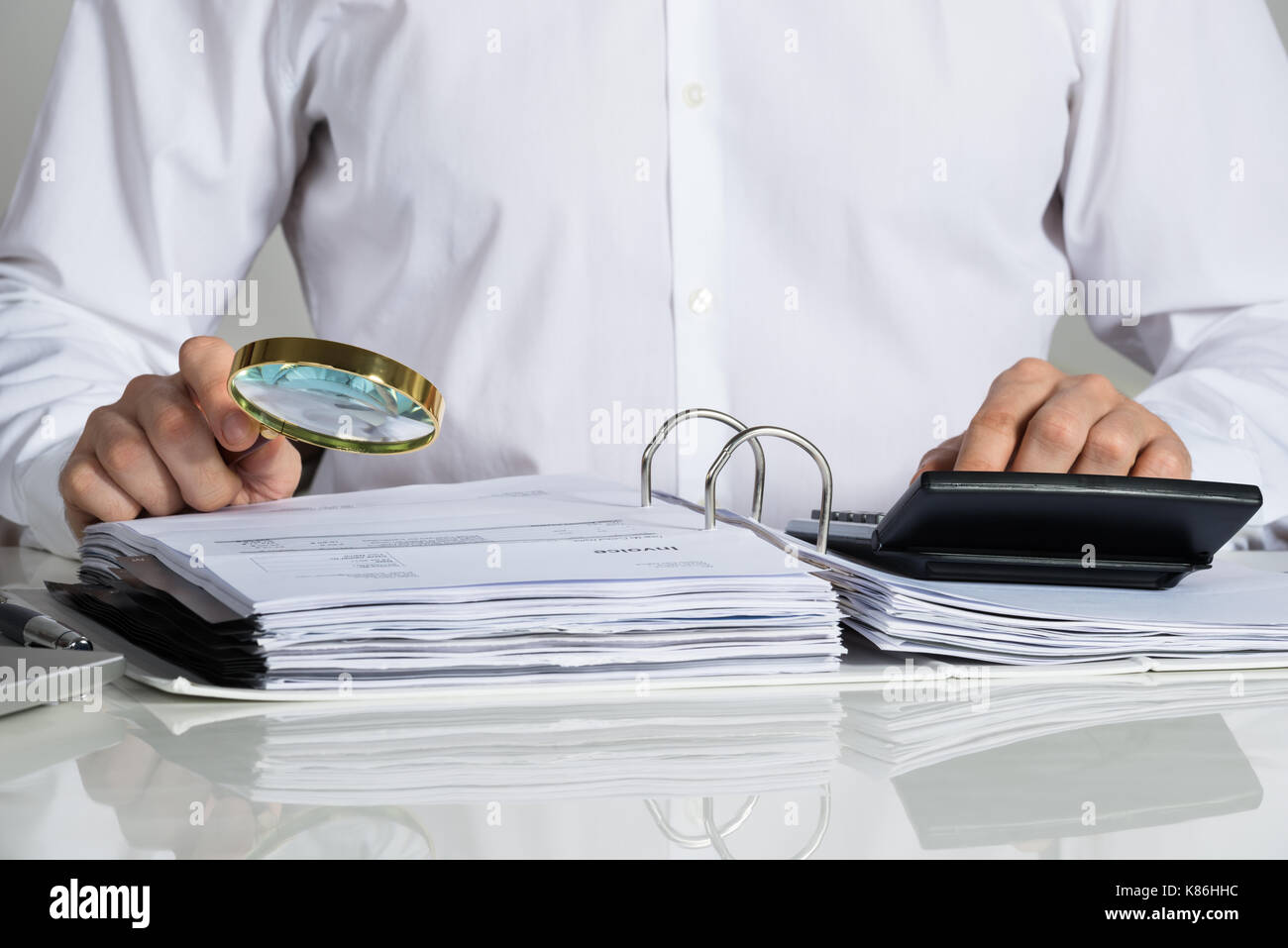 Midsection of businessman examining invoice with magnifying glass at ...