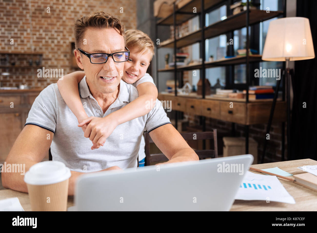 Affectionate boy hugging his father busy with work Stock Photo - Alamy