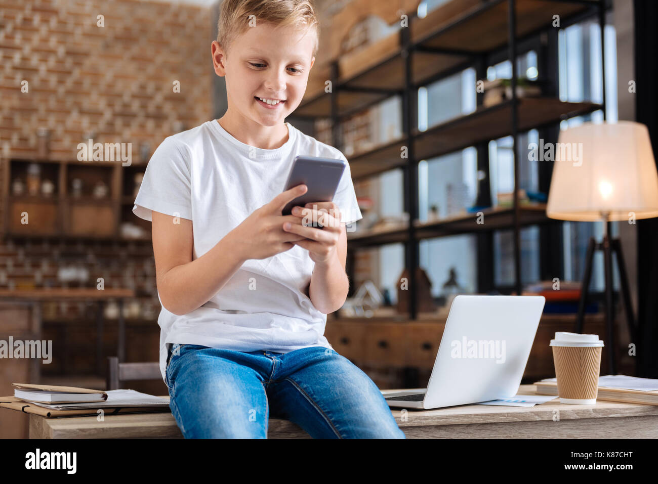 Upbeat pre-teen boy sitting on table and texting friends Stock Photo ...