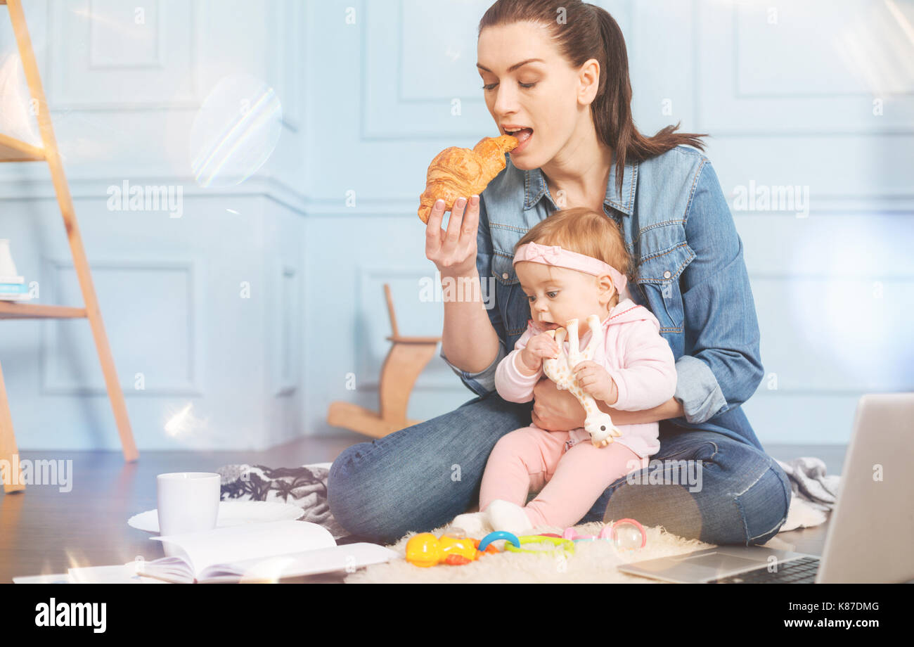 Serious brunette eating while reading book Stock Photo - Alamy