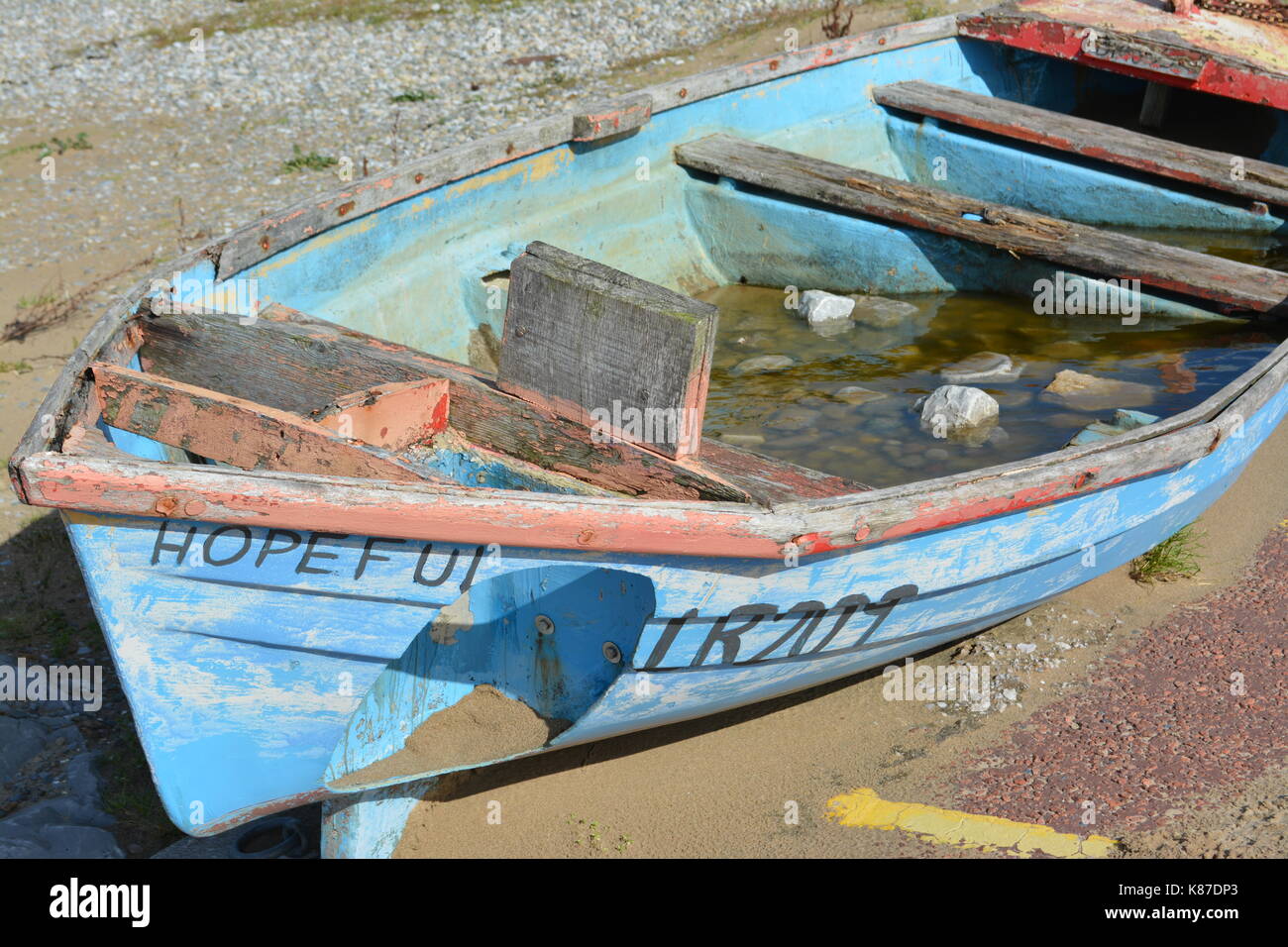 Old painted rowing boat with hole in side filled with water and rocks ...