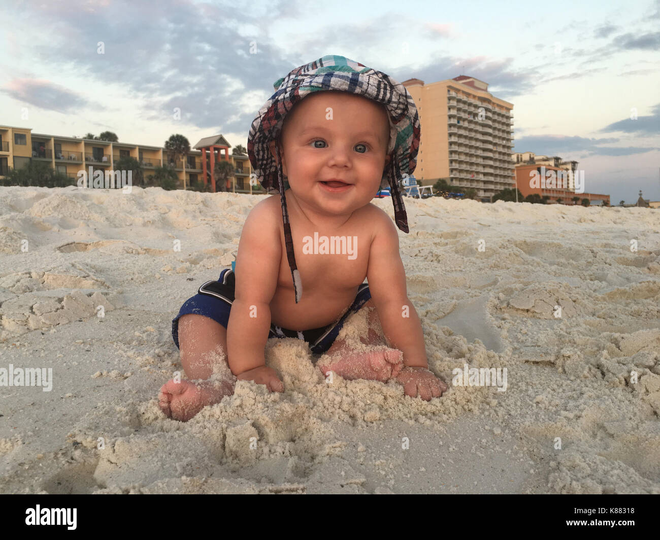 A cute, smiling, baby has a fun in the warm sand. This is his first ...