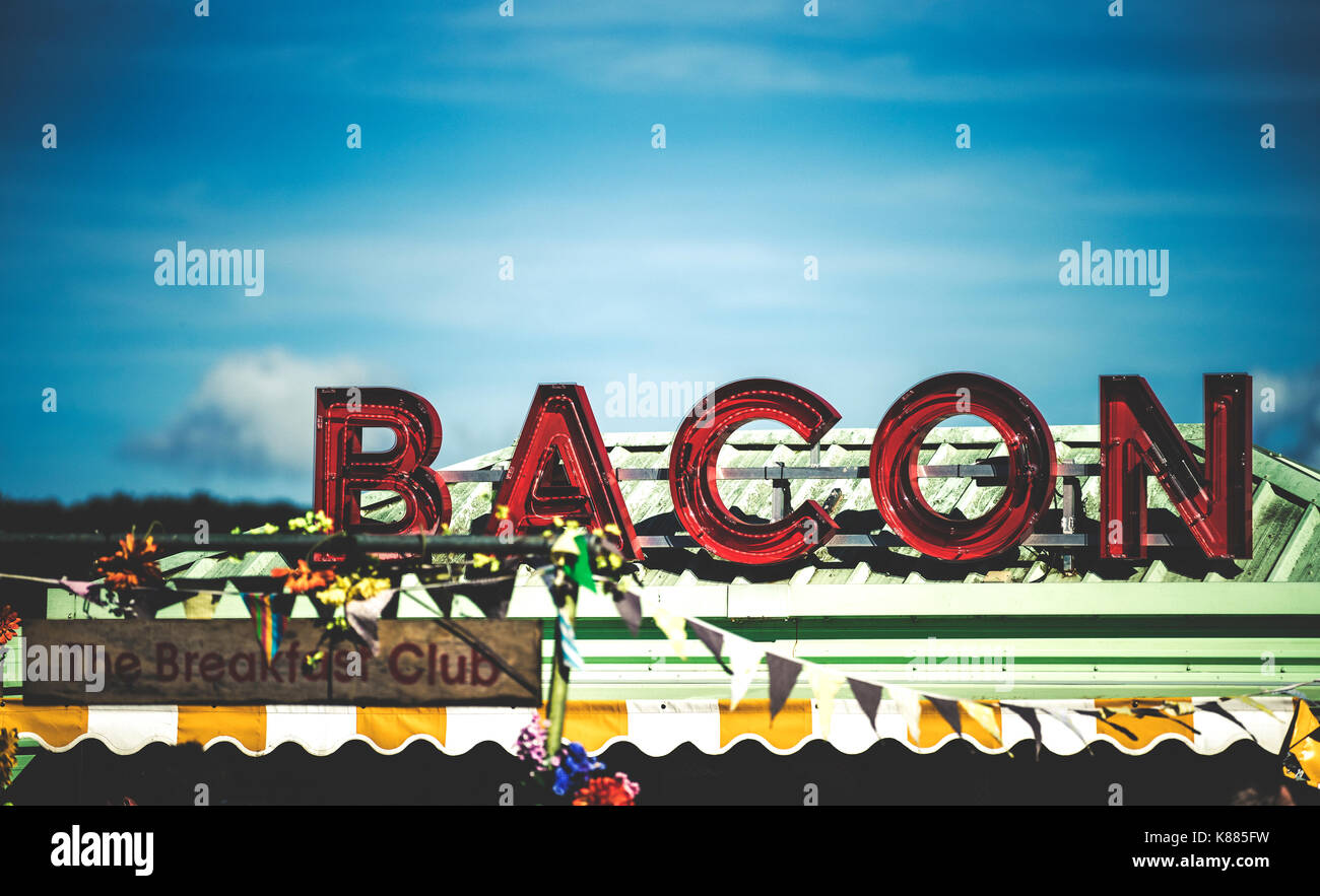 Food stall at a summer music festival red neon sign advertising bacon ...