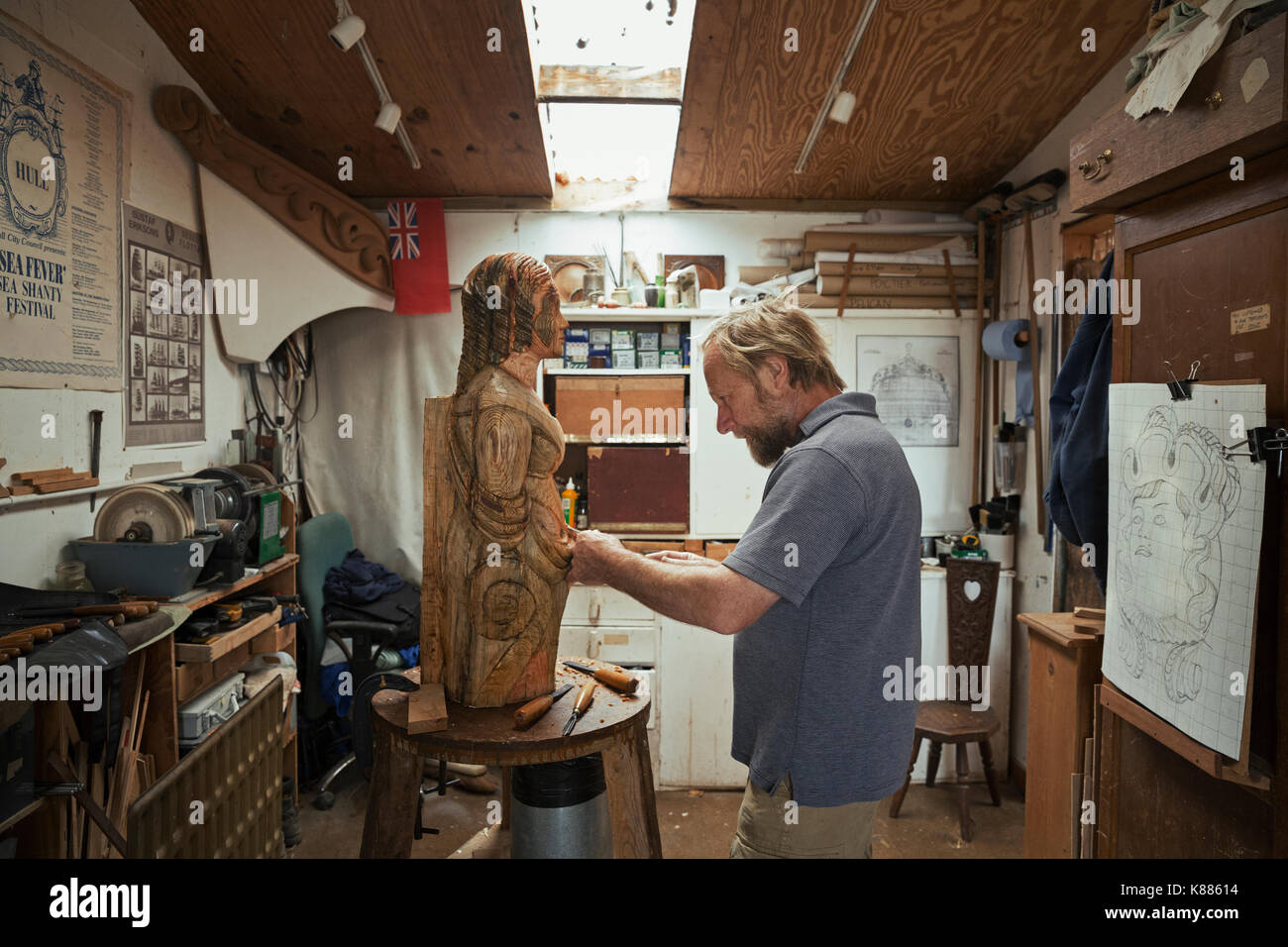 A wood carver standing in his workshop, using hand tools to shape and ...