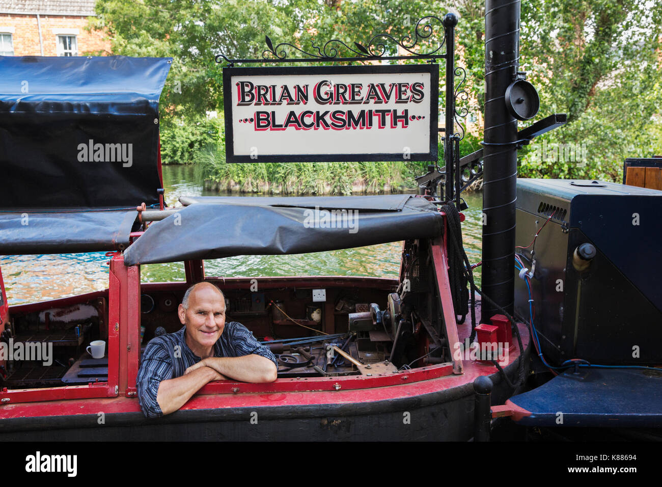 Blacksmith sitting on his working narrowboat on a waterway, looking at ...