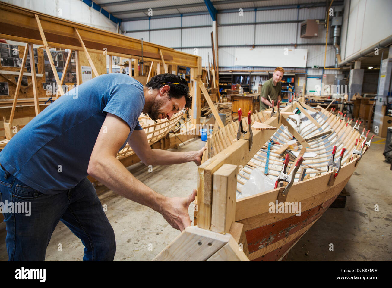 Two men in a boat-builder's workshop, working together on a wooden boat ...