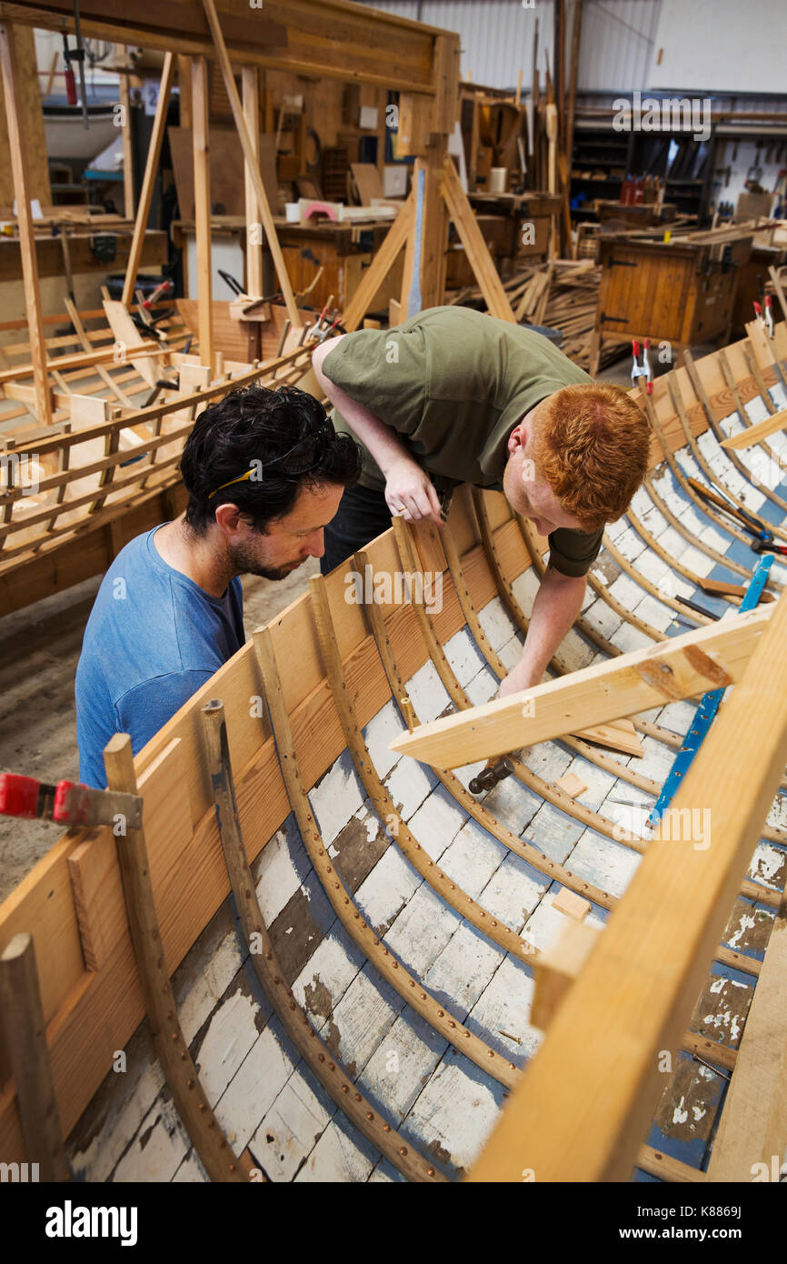 Two men in a boat-builder's workshop, working together on a wooden boat ...