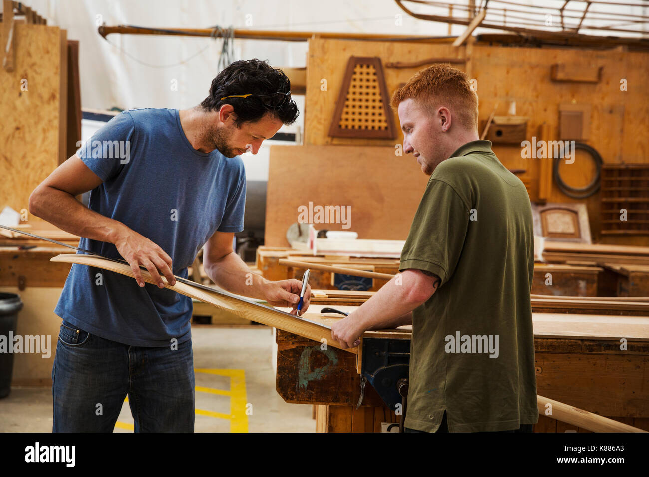 Two men standing at a workbench in a boat-builder's workshop, working ...