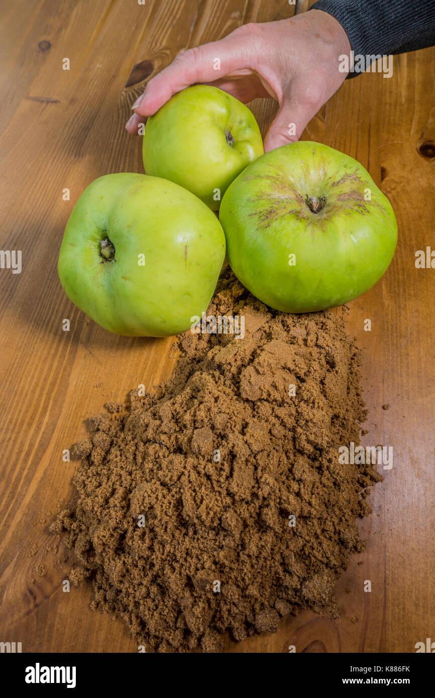 A woman's hand holding one of three raw, Bramley cooking apples ...
