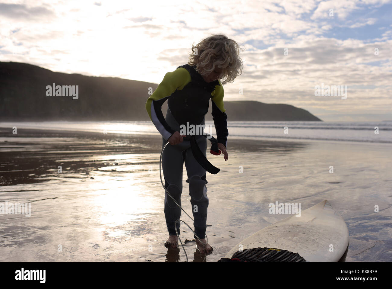 Young boy getting ready to surf with his surfboard on the beach wearing ...