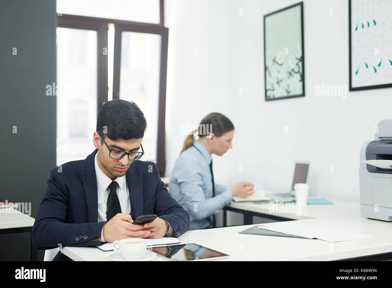 Young manager texting by workplace with colleague on background Stock ...
