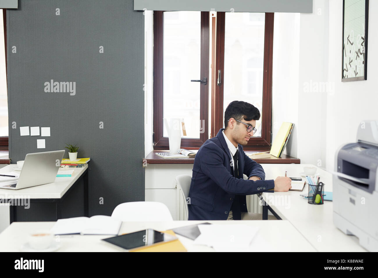 Young employee making notes in notebook while sitting by desk Stock ...