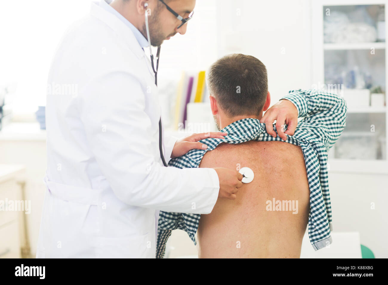 Rear view of patient sitting while doctor examining him with ...