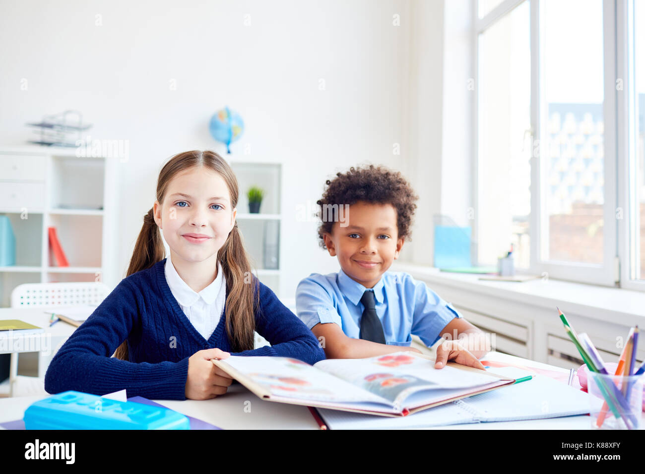 Two little classmates with open book reading in group Stock Photo - Alamy