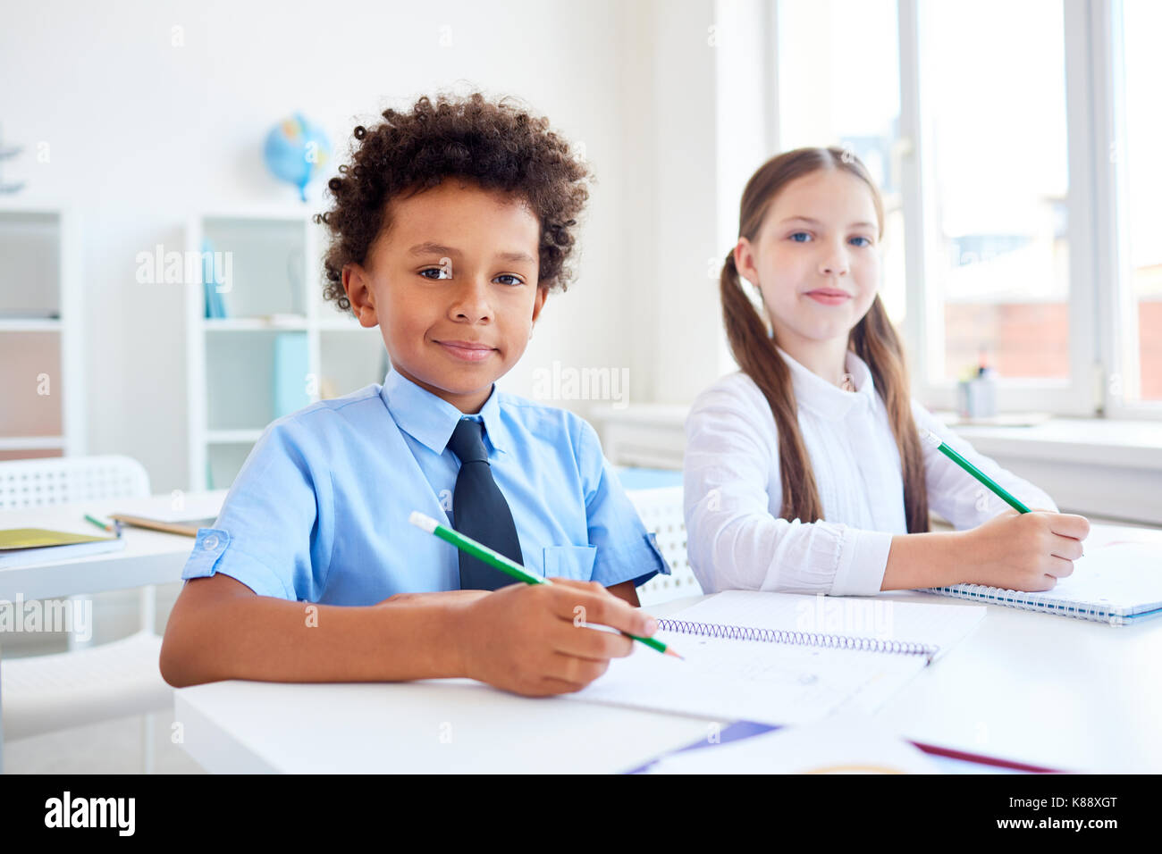 Adorable classmates with pencils drawing by desk at lesson Stock Photo ...