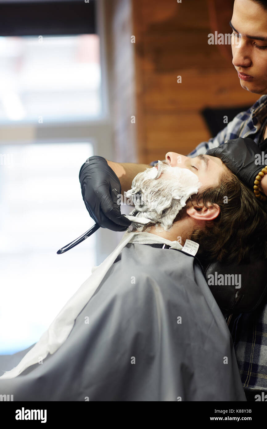Self-employed barber shaving his client with sharp dangerous razor ...