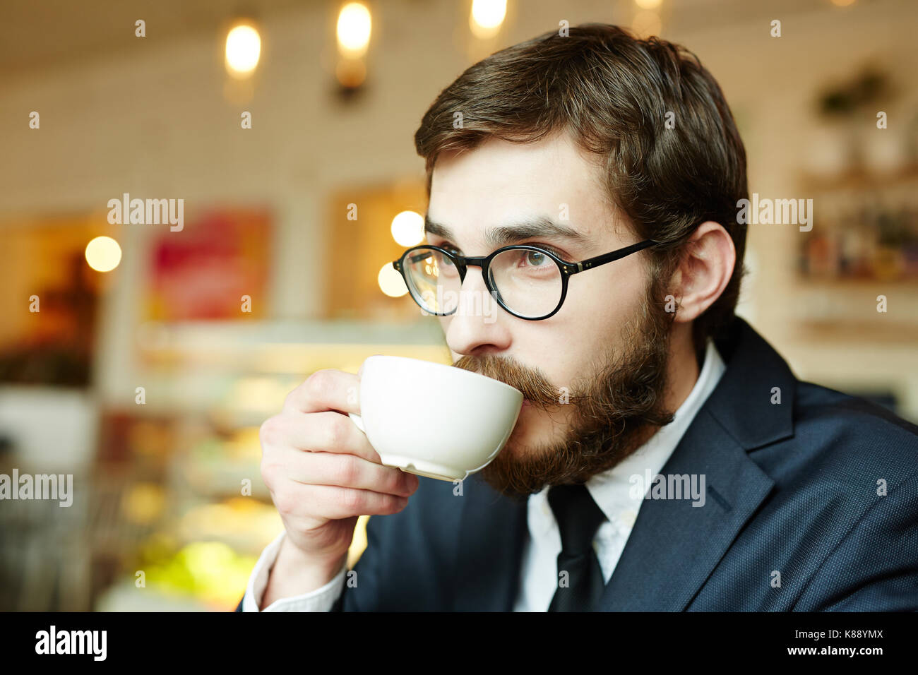 Young man in formalwear and eyeglasses drinking tea or coffee from ...